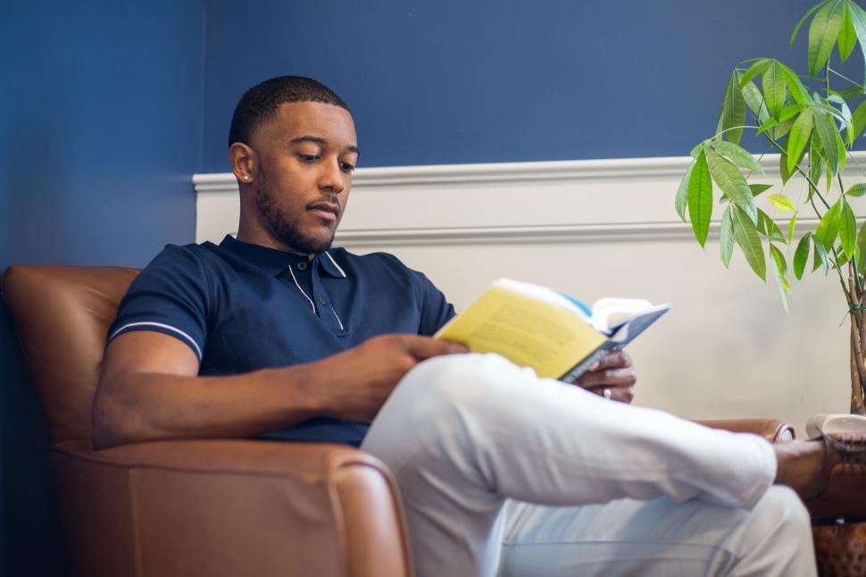 Free Stock Photo of Man reading book in brown armchair against blue ...