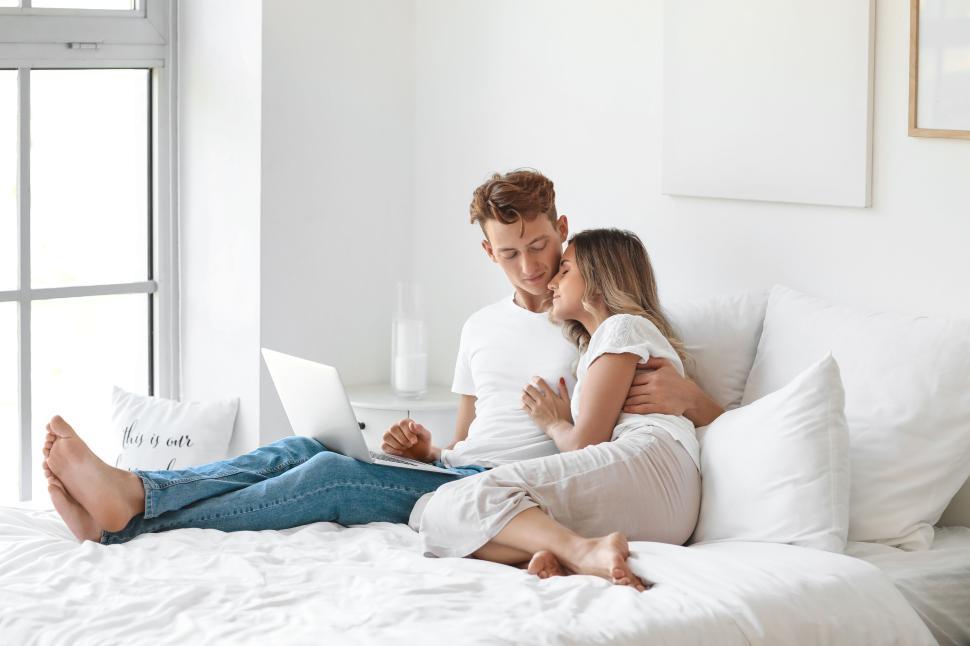 Free Stock Photo of Relaxed couple cuddling on bed with laptop in ...