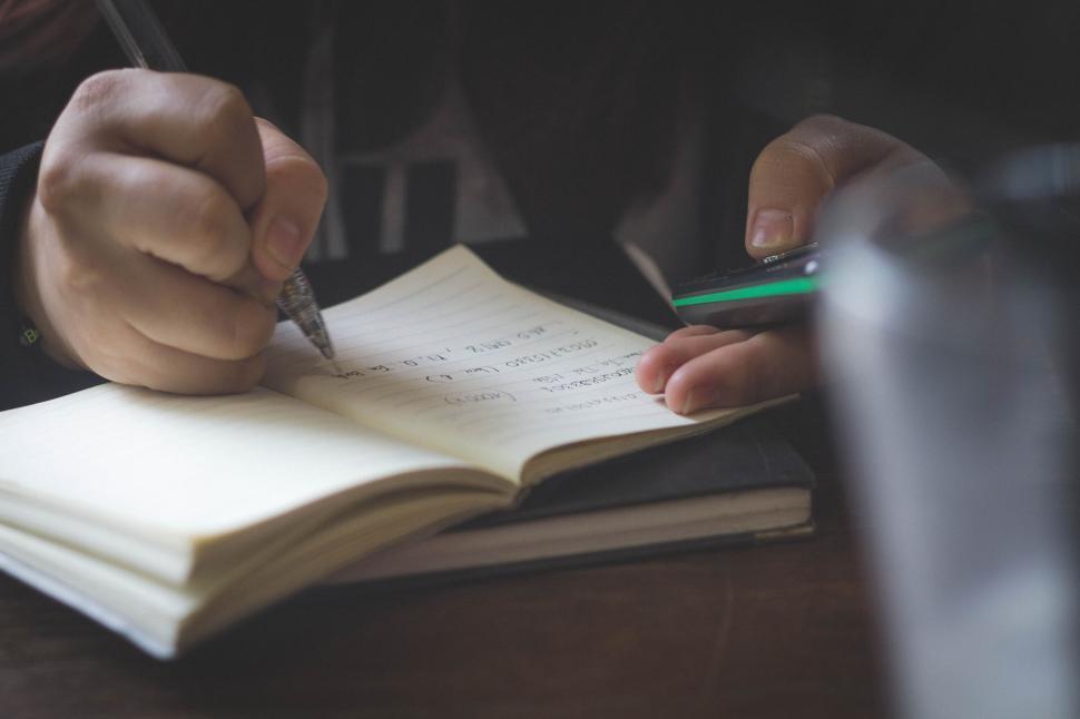 Free Stock Photo of Person writing notes with phone on table beside ...