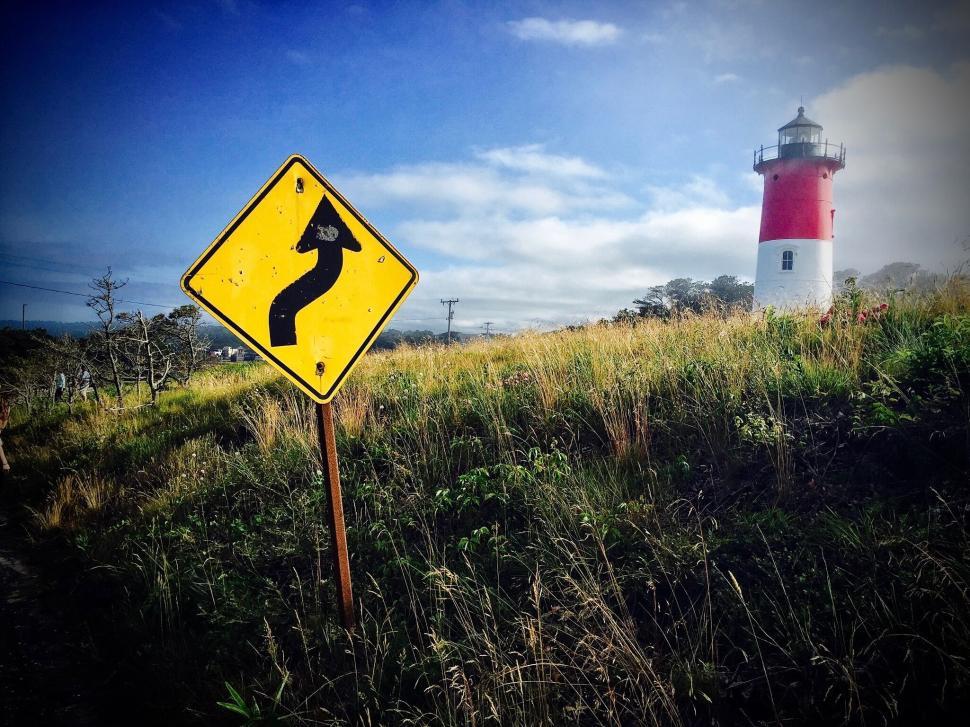Free Stock Photo of Lighthouse next to winding road sign and grassy ...