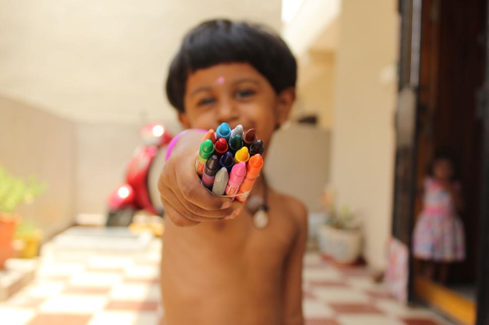 Free Stock Photo of Smiling child holding colorful crayons towards the ...