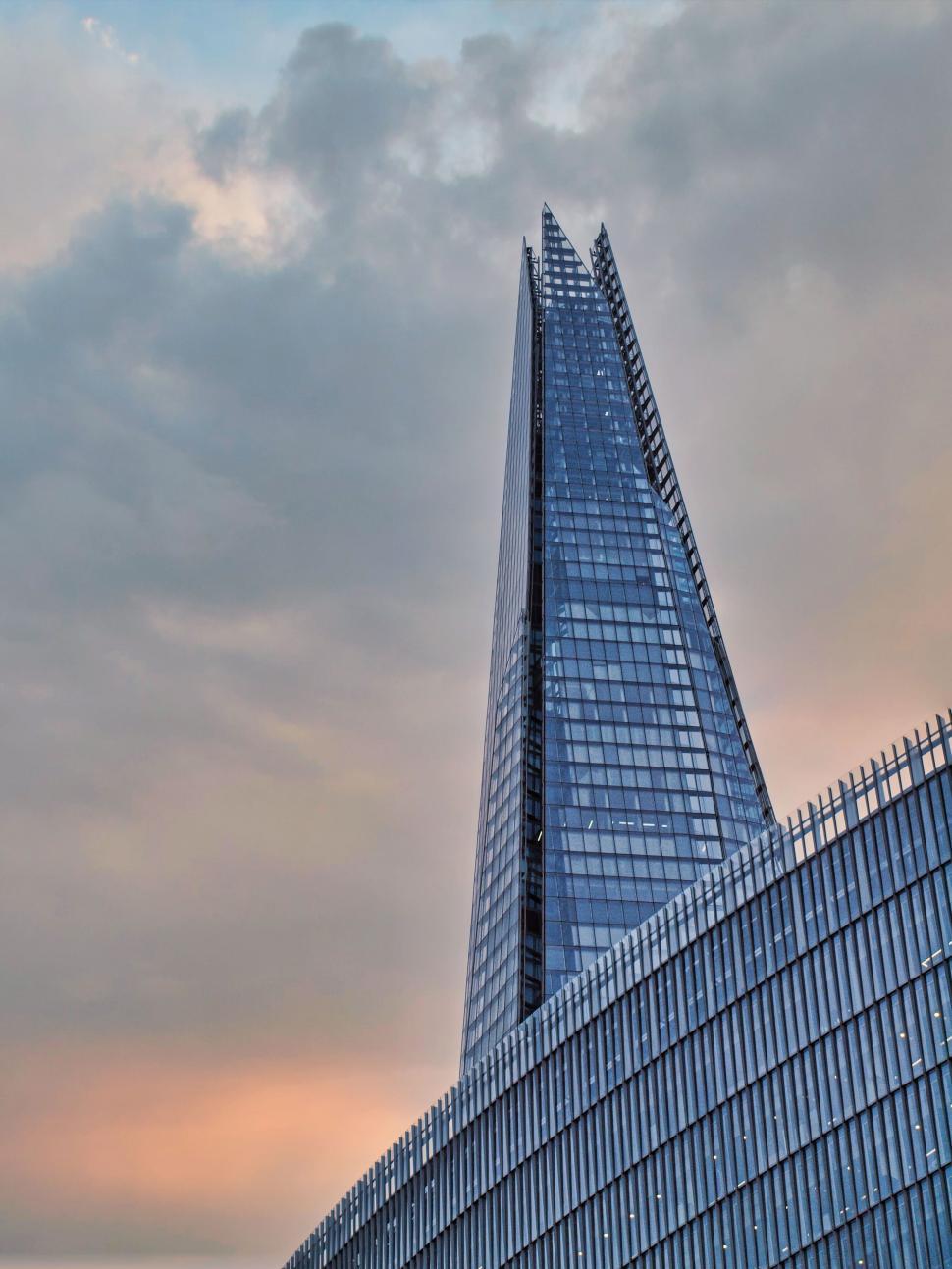 Free Stock Photo of Tall glass building with a spire under a dramatic ...