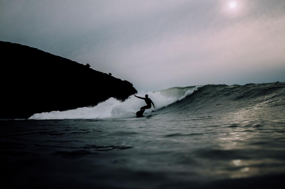 Free Stock Photo of Surfer riding a wave near rocky shore at sunset ...